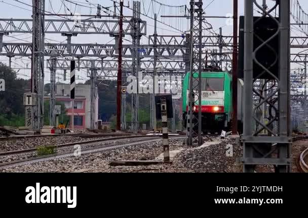 A green freight train navigates a busy railway junction surrounded by ...