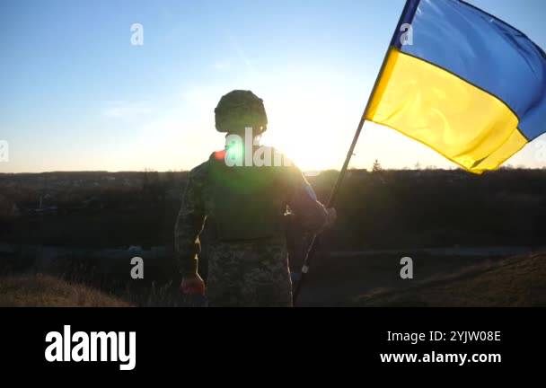 Soldier of ukrainian army stands at hill and holds waving flag of ...