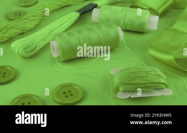 Top view of sage green cotton fabric, buttons and spools of threads ...