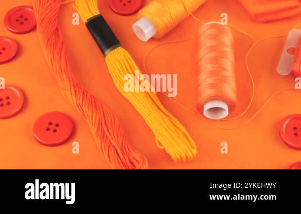 Top view of orange cotton fabric, buttons and spools of threads, floss ...