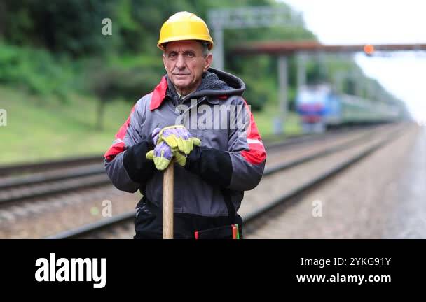 Railway man in hard hat with shovel in hands stands on railway track ...