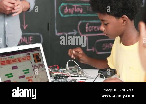 Cute african boy learning to use electronic tool while laptop display code while teacher talking ...
