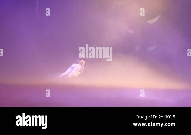 A performer on a smoke-filled stage skillfully performs an aerial act ...