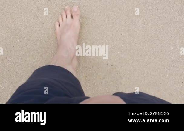 view top down to barefooted feet while walking on sandy white ocean ...