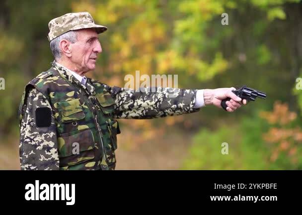 Elderly person in military uniform shoots a revolver. Retired officer ...