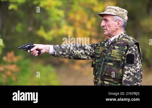 Elderly person in military uniform shoots a revolver. Retired officer ...