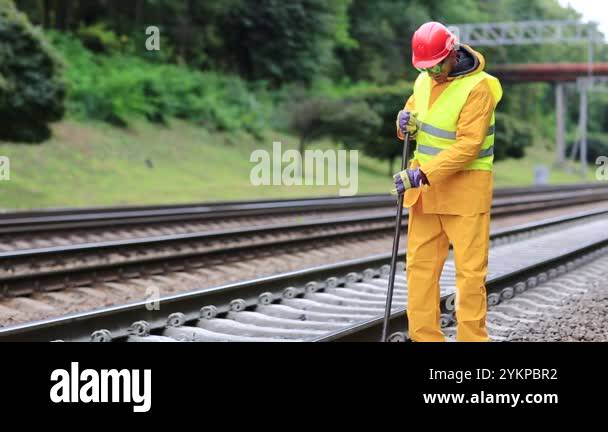 Railway worker in yellow uniform with crowbar in hands mends railway ...