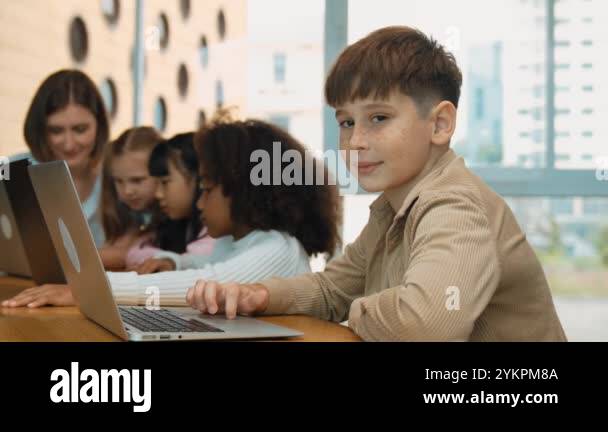 Boy looking at camera with multicultural friend learning prompt at STEM technology class ...