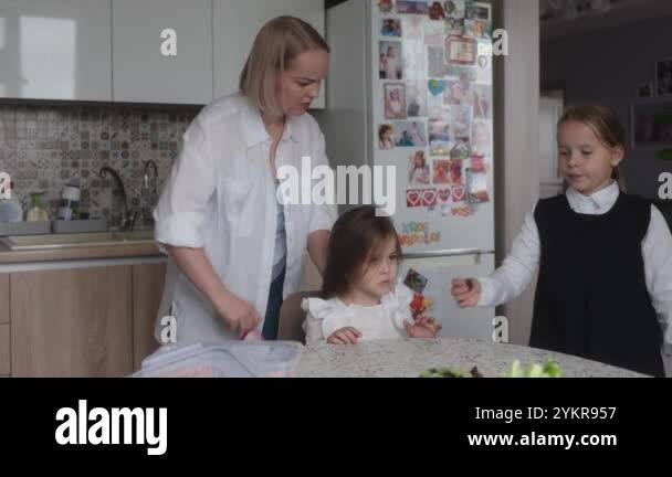 A mother combs her daughters hair in the kitchen as she prepares her for school. The other ...