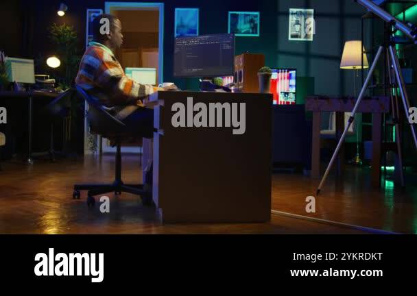 Programmer in home office concentrating on finding bugs while he codes on his computer. African ...