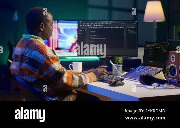 Programmer in home office concentrating on finding bugs while he codes on his computer. African ...