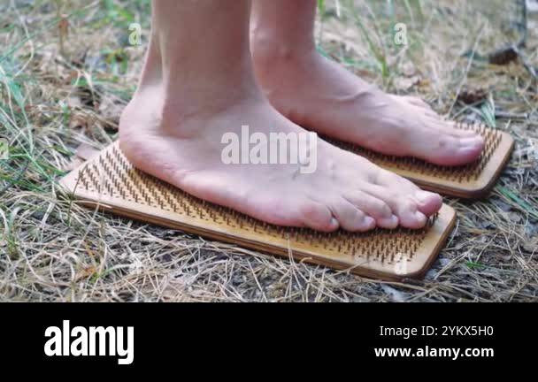 Barefoot man steps on a wooden spiky acupressure board in nature ...