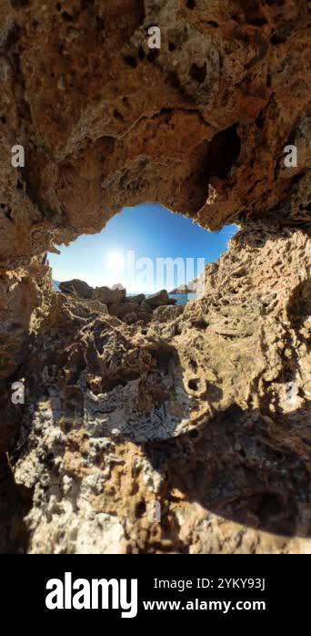 Vertical video. A view from inside a rock cave opening to the sunlit ...