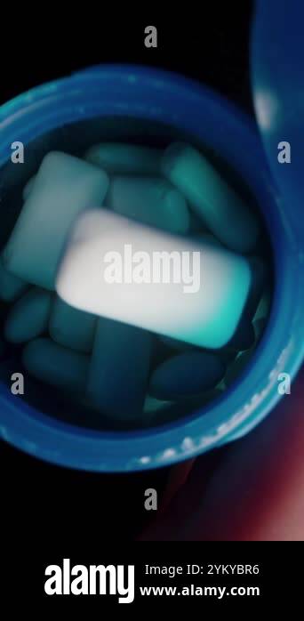 Vertical video. In slow motion, a single white gum tablet falls into an ...