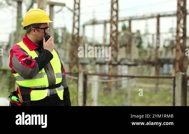 Workman with portable radio transmitter on electric power station ...