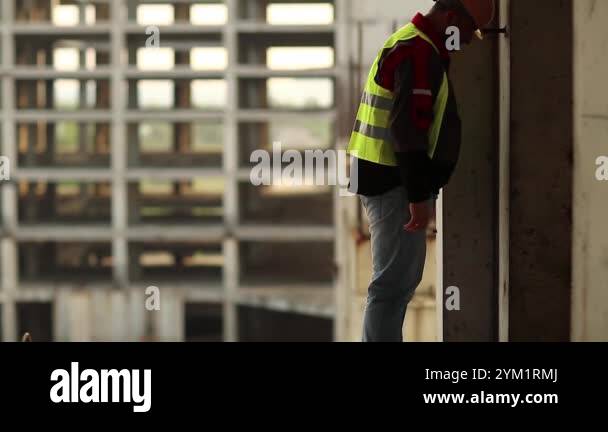 Stressed builder in hard hat stands on construction site and knocks his ...