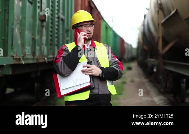 Railway worker talks on mobile phone between goods trains. Chief of ...
