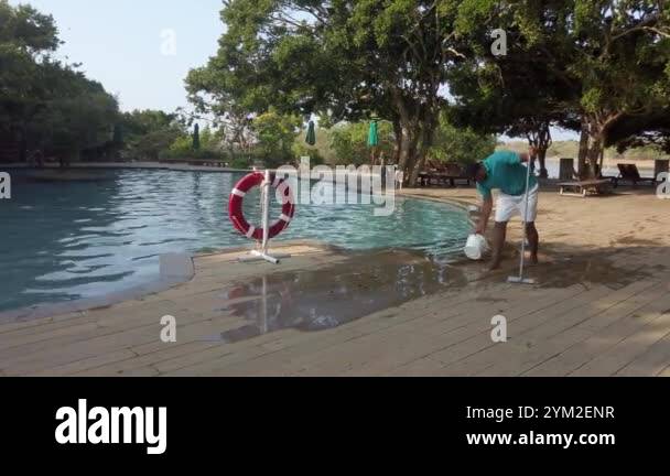 Hotel employee cleaning the pool deck at a tropical resort, ensuring a ...