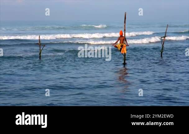 Sri lankan fisherman in an orange turban balances on a stilt in the ...