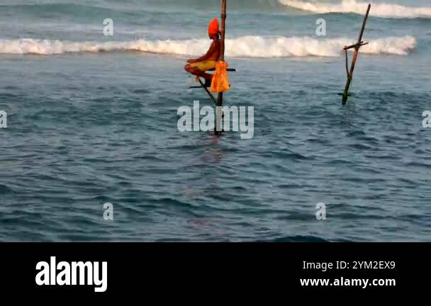 Sri lankan fisherman wearing an orange turban balances on a stilt while ...