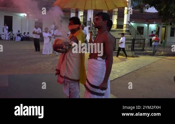 Two hindu priests wearing dhotis are burning incense and praying in a temple courtyard in ...