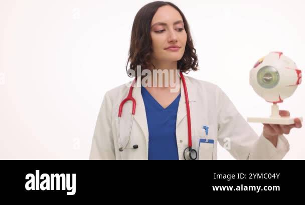 Woman ophthalmologist holds artificial eye model and pair of glasses in hands on white ...
