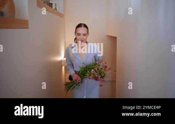 Romantic woman carrying bouquet entering home alone closeup. Young tender lady holding bunch of ...