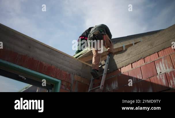 Construction workers descending ladder from rooftop, safety equipment ...