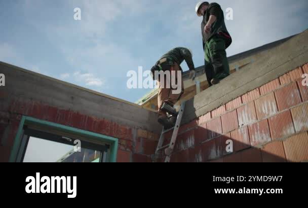 Construction worker descending ladder from rooftop on building site ...