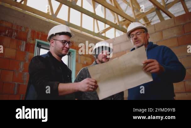 Construction workers reviewing blueprints in partially built structure ...