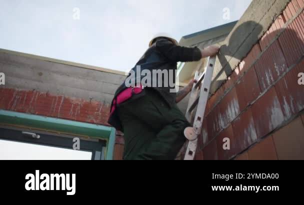 Two construction workers ascending ladder on building site, securing ...