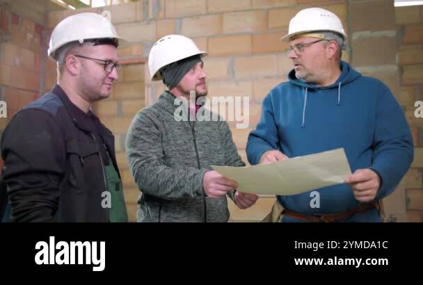 Team of builders reviewing blueprints together indoors, construction ...