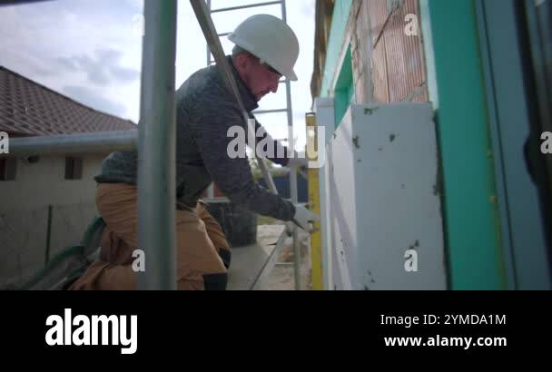 Construction worker using spirit level to align insulation panel on wall, focused on precision ...