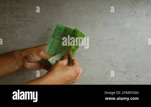 Person counting malaysian ringgit against a concrete wall, showcasing ...