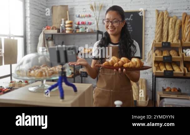 Young woman recording a video for social media while holding pastries in a bakery shop in china ...