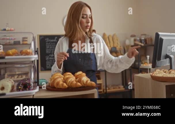 Woman working in bakery room arranging pastries on display behind ...