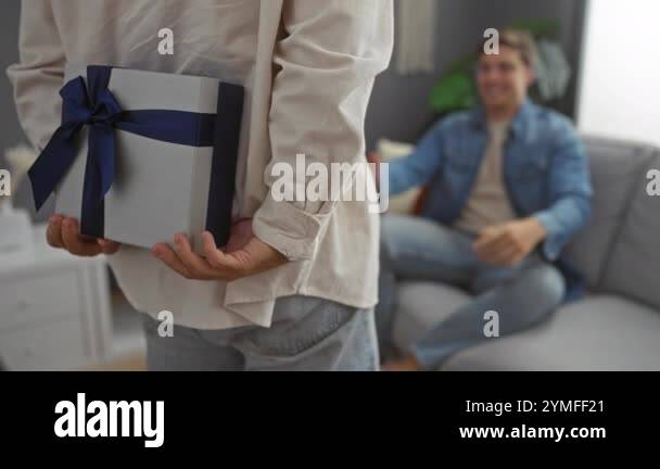 Two men, friends in an indoor home setting, exchange a gift with one ...