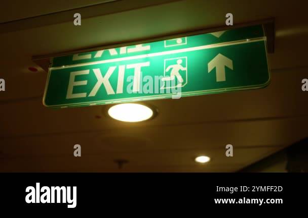Bright illuminated exit sign indoors with green background and ...