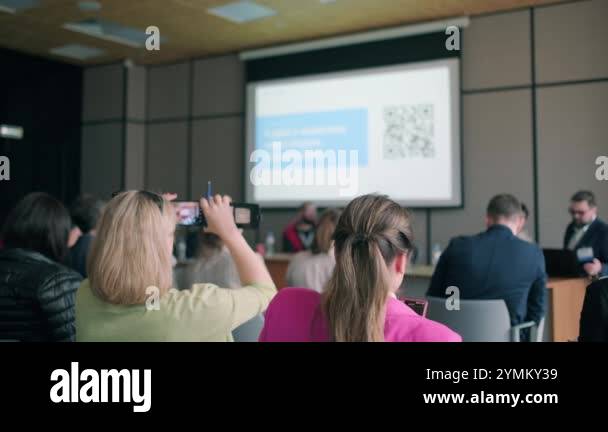 Real time soft focus of people sitting in conference hall scanning QR ...