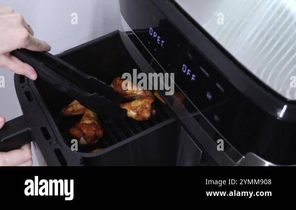 Turning chicken wings with tongs in air fryer, ensuring even roasting ...