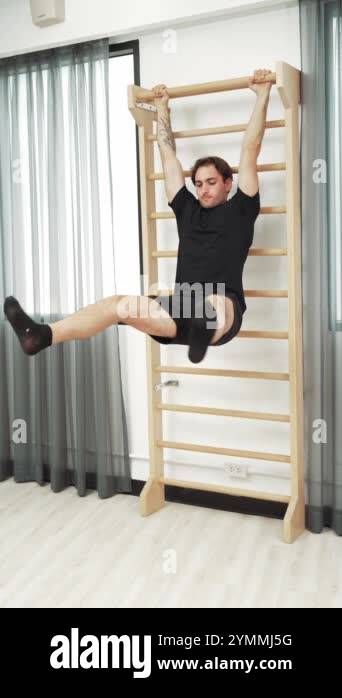 Happy man doing hanging leg raise exercise on wall bars to strengthen core muscles and improve ...