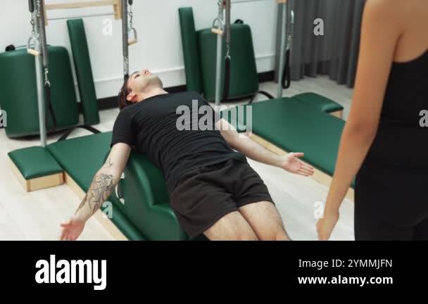 Male client practicing leg lifts on Pilates arc barrel with instructor ...
