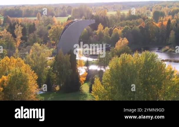 A unique curved observation tower stands in a lush forest with golden ...
