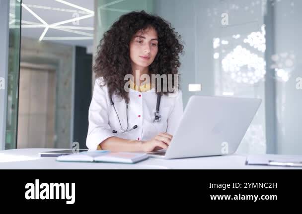 Focused young female doctor is using, typing on a laptop while sitting ...