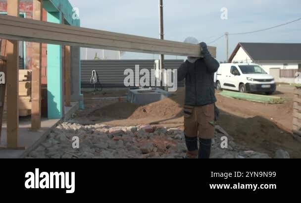 Construction worker moving long wooden beams on shoulder at building ...
