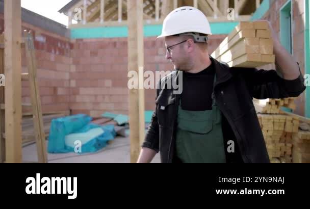 Construction worker carrying stack of wooden planks, preparing materials for framing at building ...