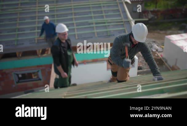 Construction worker hammering roof beams while colleagues observe ...
