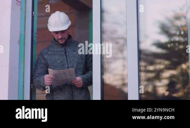 Construction worker holding blueprints in doorway, inspecting plans ...