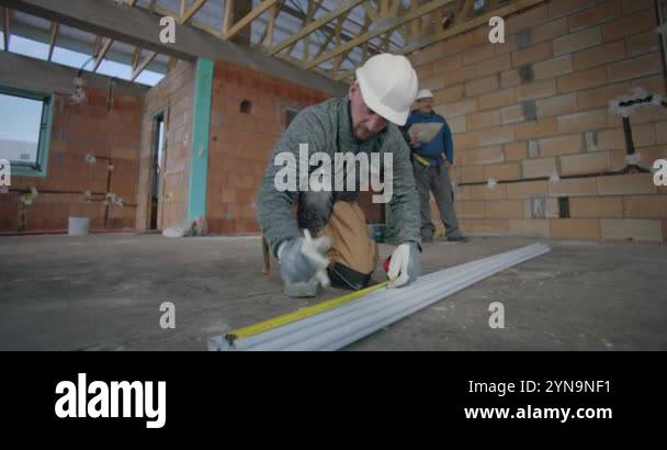 Construction worker using tape measure on pipes while colleagues review ...