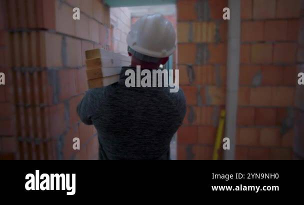 Construction worker carrying wooden beam on shoulder, navigating ...